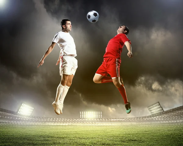 Two football players in jump to strike the ball at the stadium — Stock ...