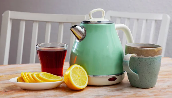 Cute electric kettle, two different cups with tea and sliced lemon on ...