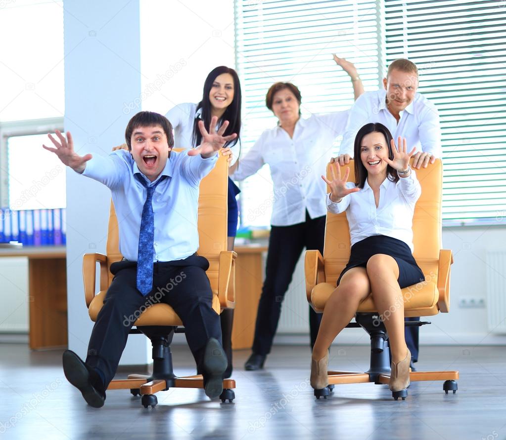Happy office employees having fun at work in an office chair race ...