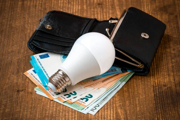 Wallet with a Euro currency and LED light bulb on the table. Concept of ...