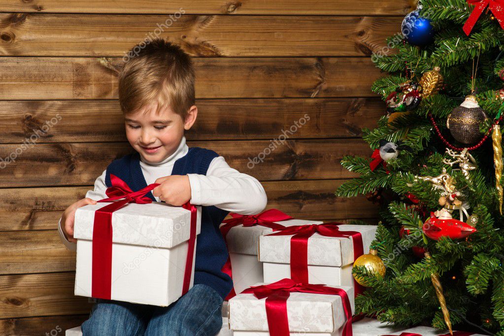 Little boy opening gift box under christmas tree in wooden house ... Little boy opening gift box under christmas tree in wooden house ...