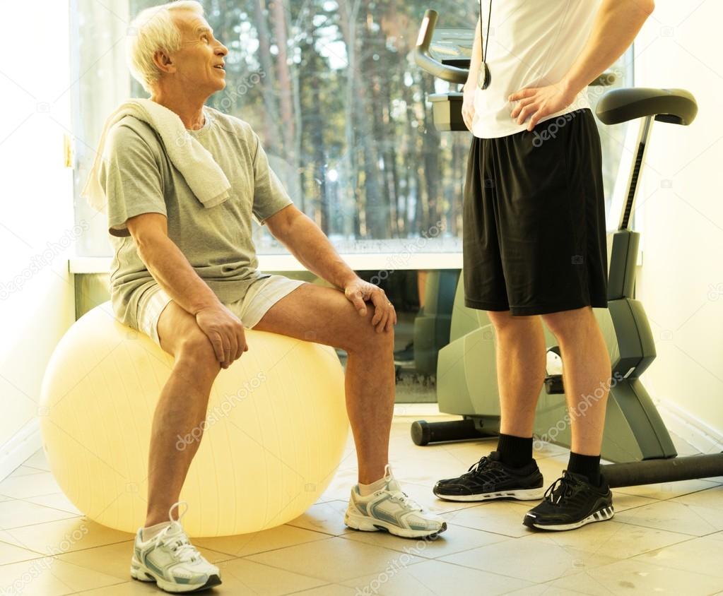 Personal trainer explains to a senior man how to do exercise on a ...