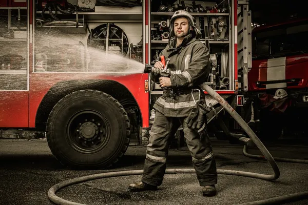 Firefighter holding water hose near truck with equipment - Stock Image ...