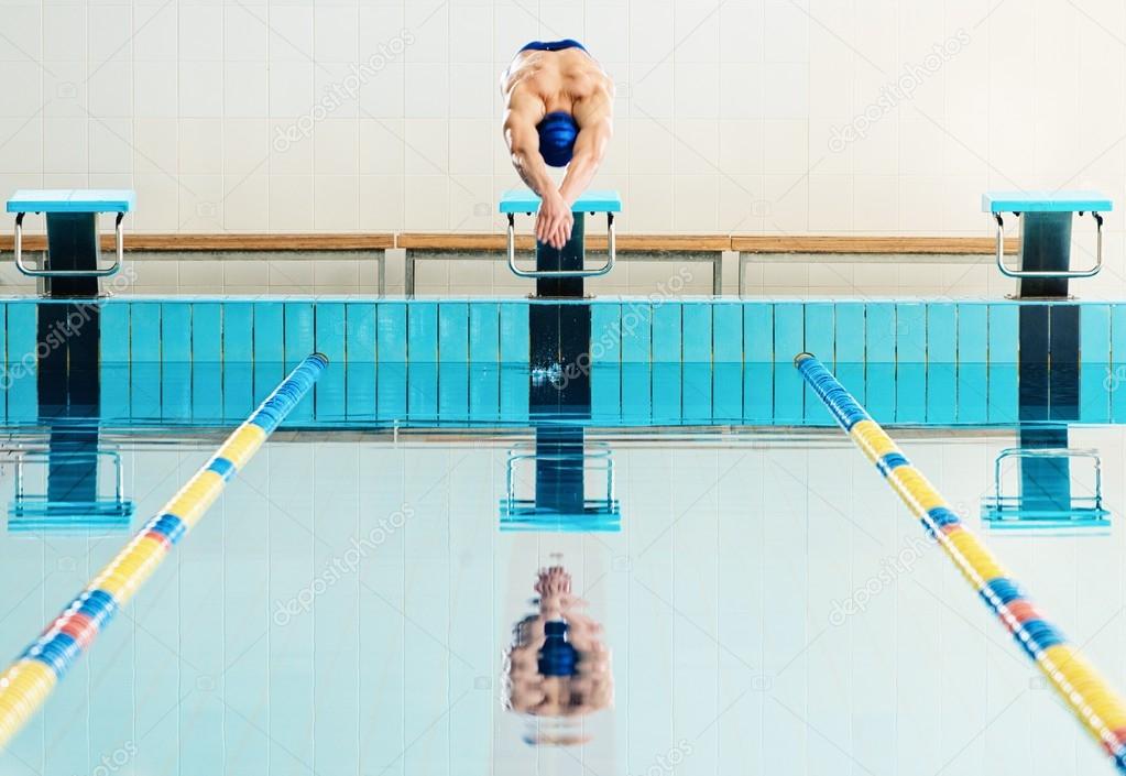 Jeune nageur musclé sautant du bloc de départ dans une piscine image ...