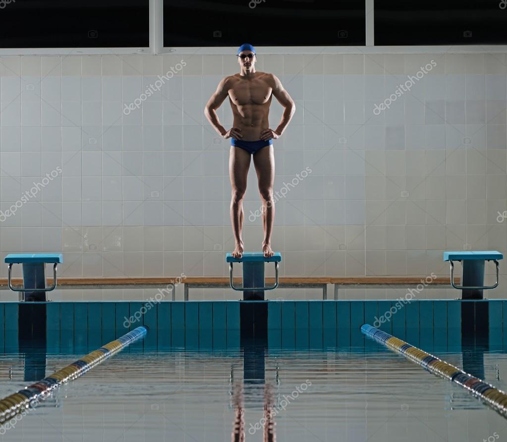 Young muscular swimmer standing on starting block in a swimming pool ...