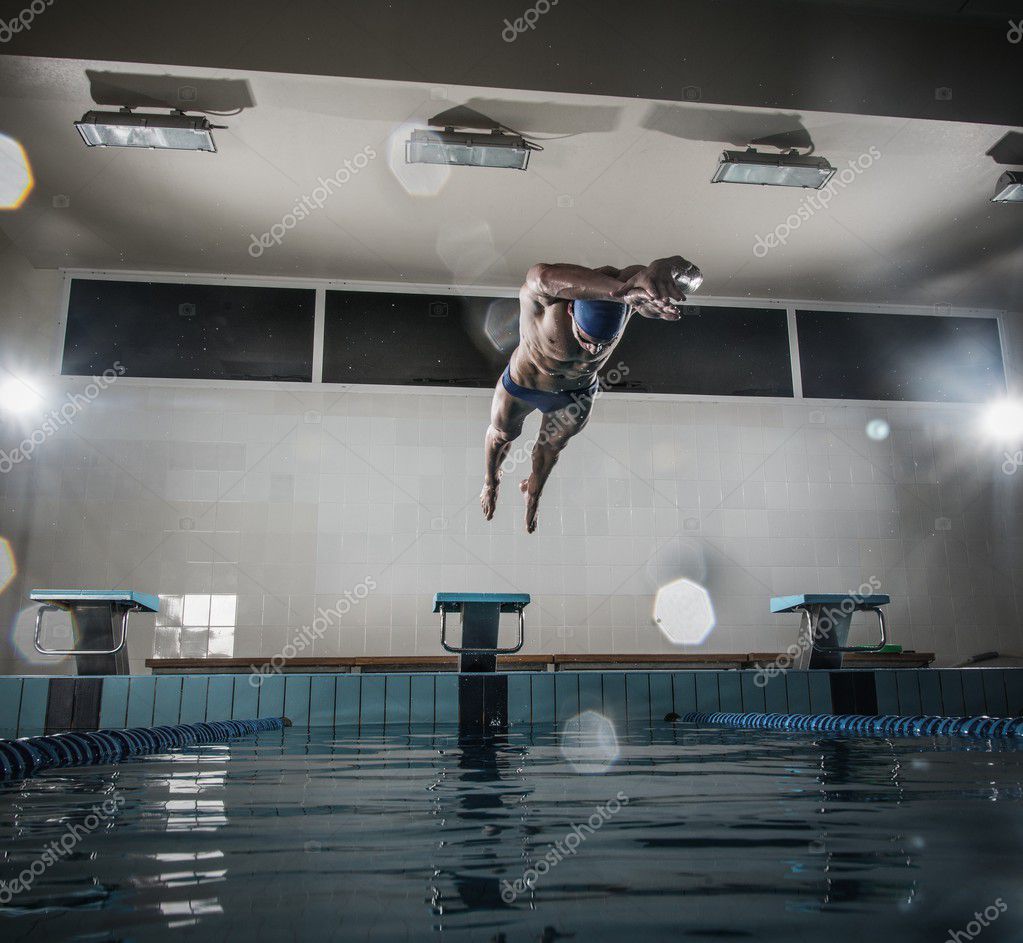 Young muscular swimmer jumping from starting block in a swimming pool ...