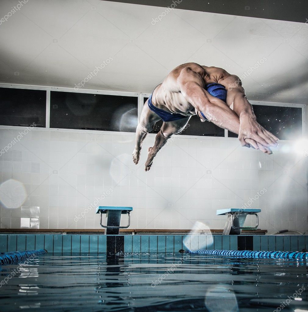 Young muscular swimmer jumping from starting block in a swimming pool ...