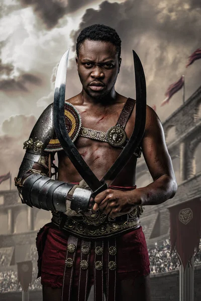 Shot of furious african gladiator holding two swords in cross in arena ...