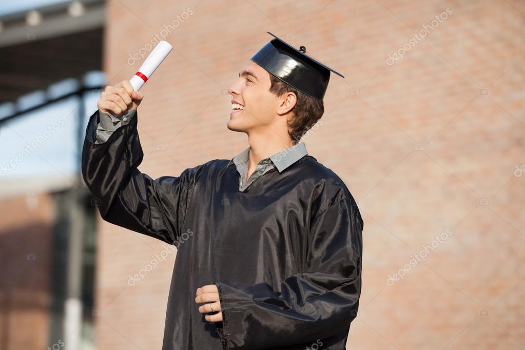 hombre de toga de graduación mirando certificado en el campus — Foto de ...
