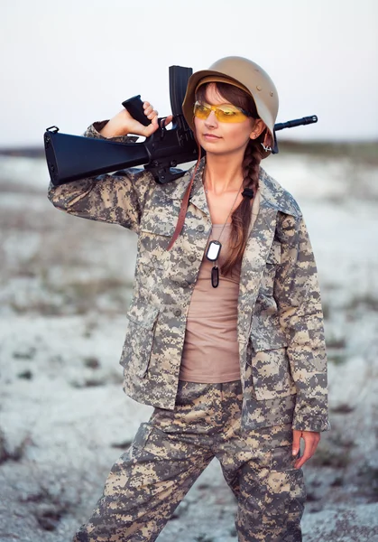 Young female soldier dressed in a camouflage with a gun in the o ...