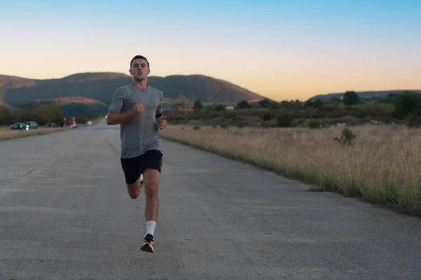 Attractive fit man running fast along countryside road at sunset light ...