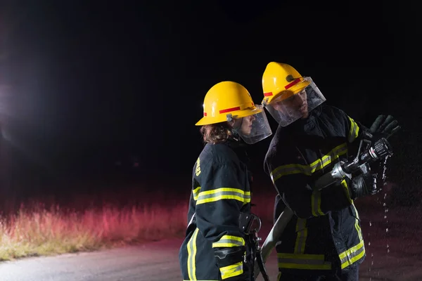 Firefighters using a water hose to eliminate a fire hazard. Team of ...