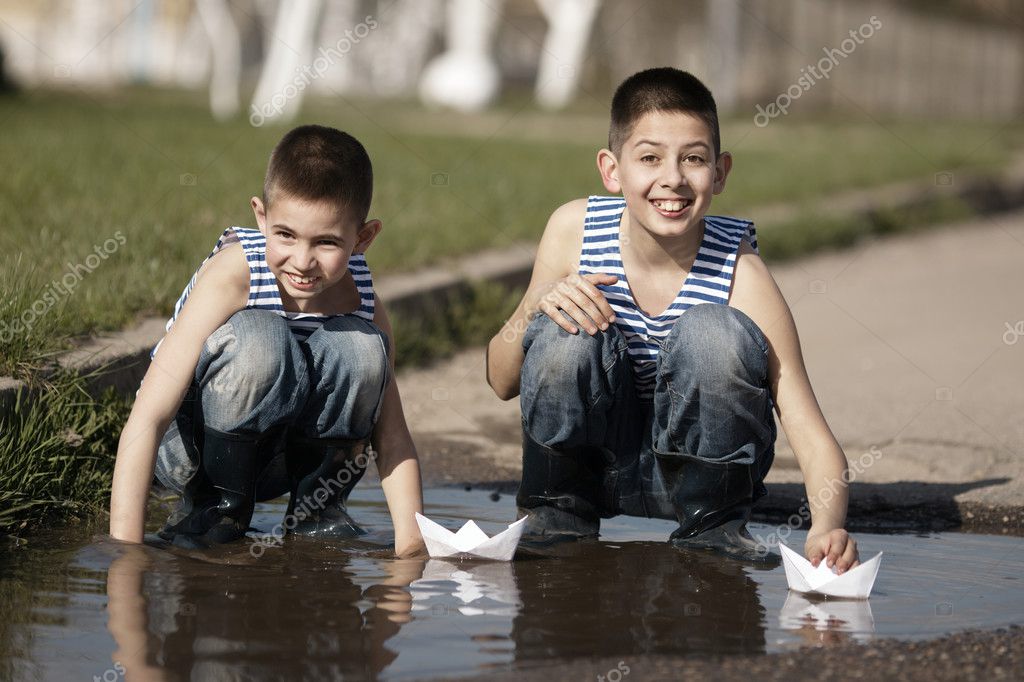 niños jugando con barcos de papel en charco 2023