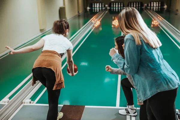 Rear view of a young woman throwing the bowling ball while her friends ...
