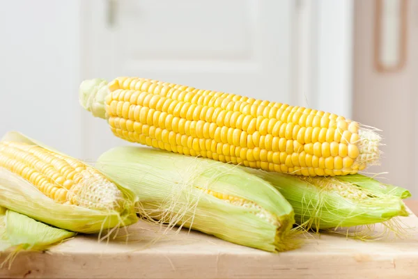 A sheaf of corn in leaves and peeled on a wooden board. Two pieces ...