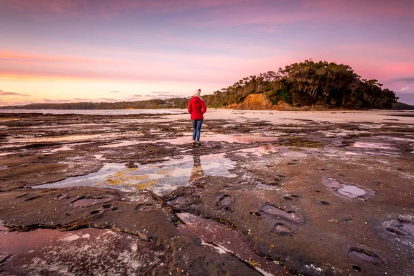Woman watches the pretty sunrise unfold standing on the outer rocky reef in low tide ...