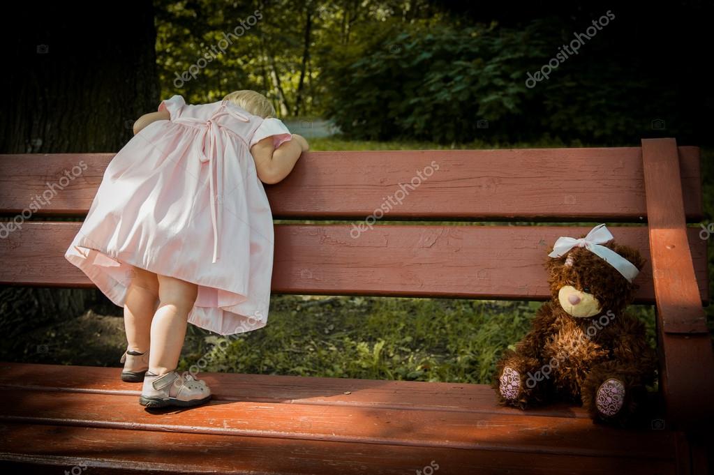 Little girl with a teddy bear is turning his back on the bench — Stock ...