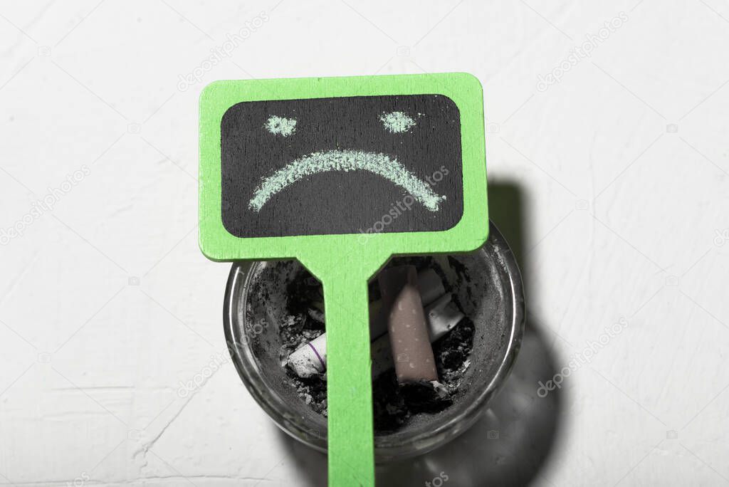 Daño al concepto de fumar. Sonriente infeliz y cenicero con colillas de ... Daño al concepto de fumar. Sonriente infeliz y cenicero con colillas de ...