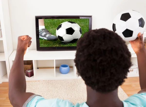 African Young Man Watching Television Holding Football - Stock Image ...