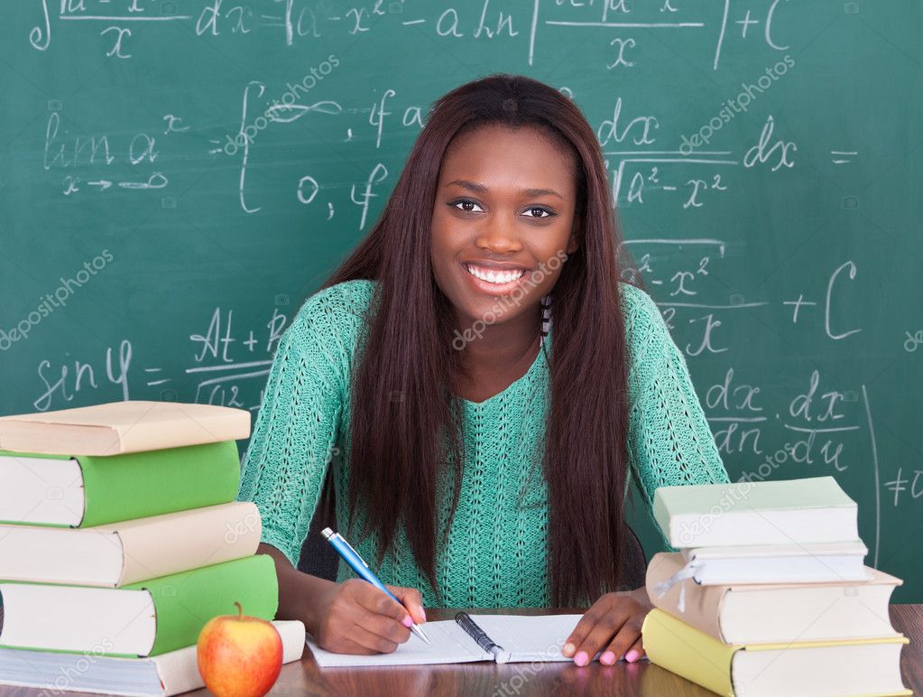 Confident female teacher writing in book at classroom desk Stock Photo ...