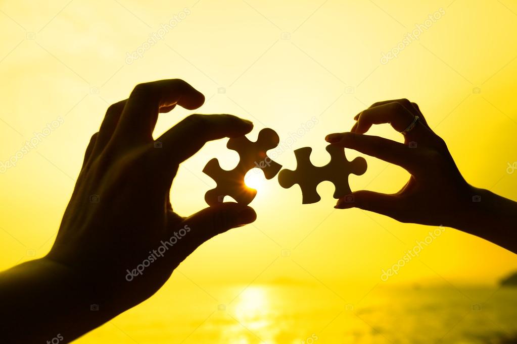 Two hands trying to connect puzzle pieces with sunset background ...
