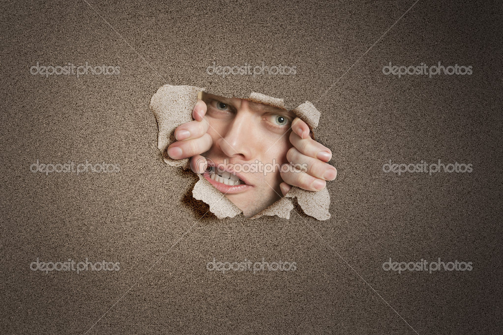 Portrait of a aggressive mid adult man peeking from ripped white paper ...