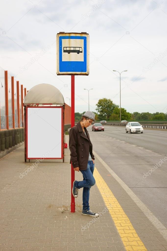 Teen boy standing at a bus stop, in the background billboard ...