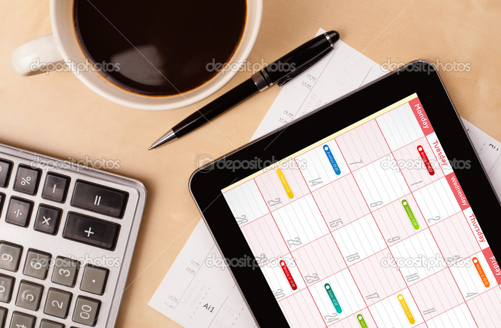 Tablet pc showing calendar on screen with a cup of coffee on a d ...