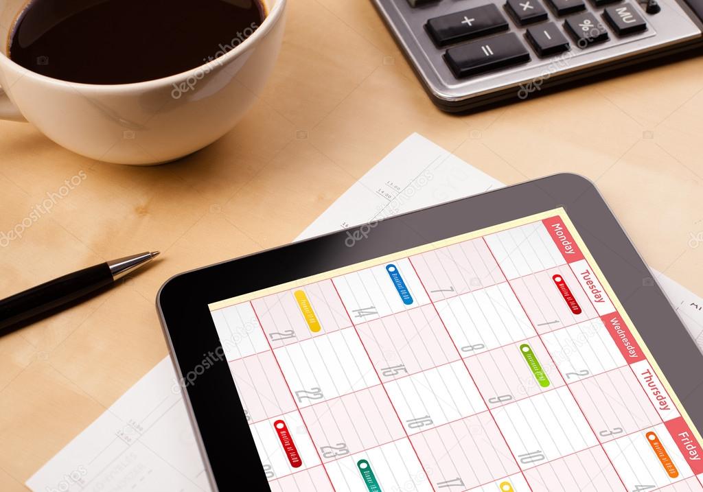 Tablet pc showing calendar on screen with a cup of coffee on a d ...