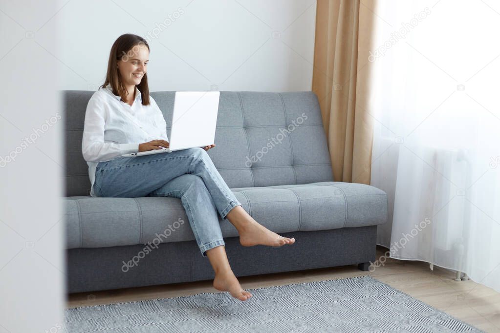 Retrato de mujer atractiva adorable con camisa blanca y jeans sentados ...