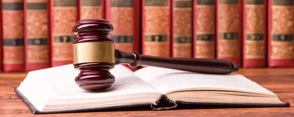 Law concept - Open law book with a wooden judges gavel on table in a ...