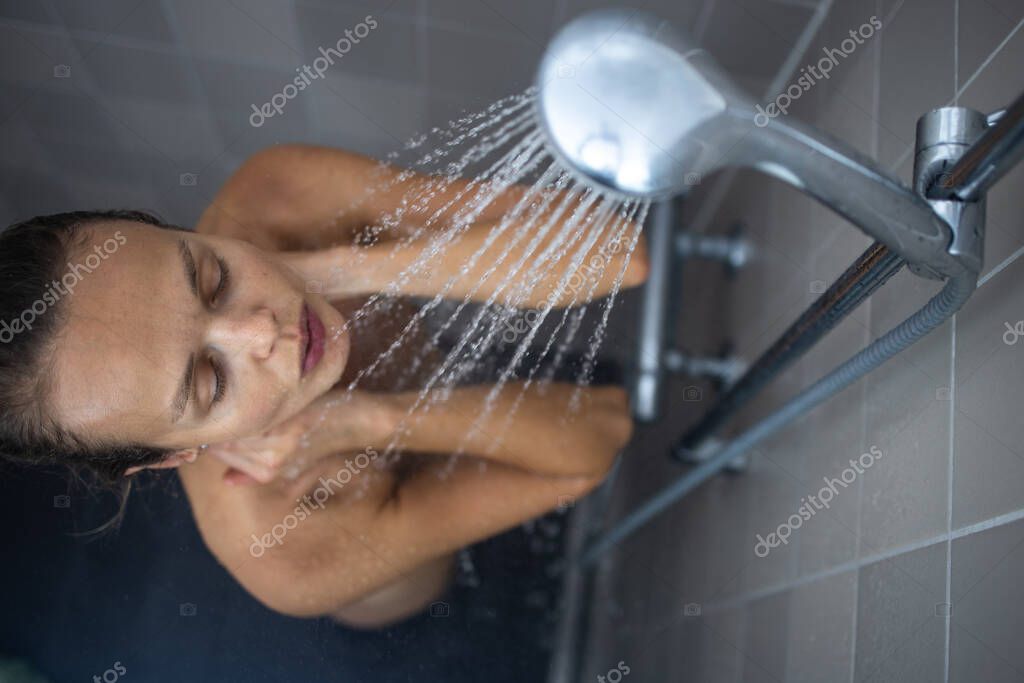 Mujer bonita y joven tomando una larga ducha caliente lavándose el cabello en un baño de diseño ...