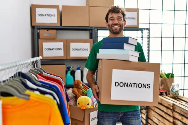 Young hispanic volunteer man smiling happy holding donations box and ...