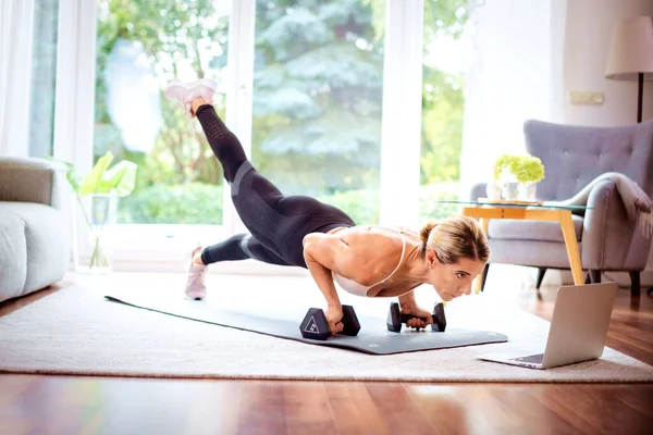 Shot of a woman using dumbbells while doing body workout at home. Woman ...