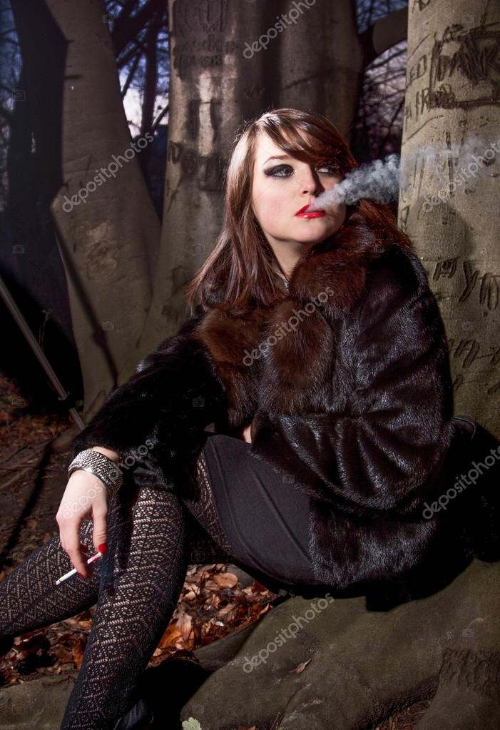 Woman In Fur Coat Smoking Cigarette While Sitting Near Big Tree — Stock