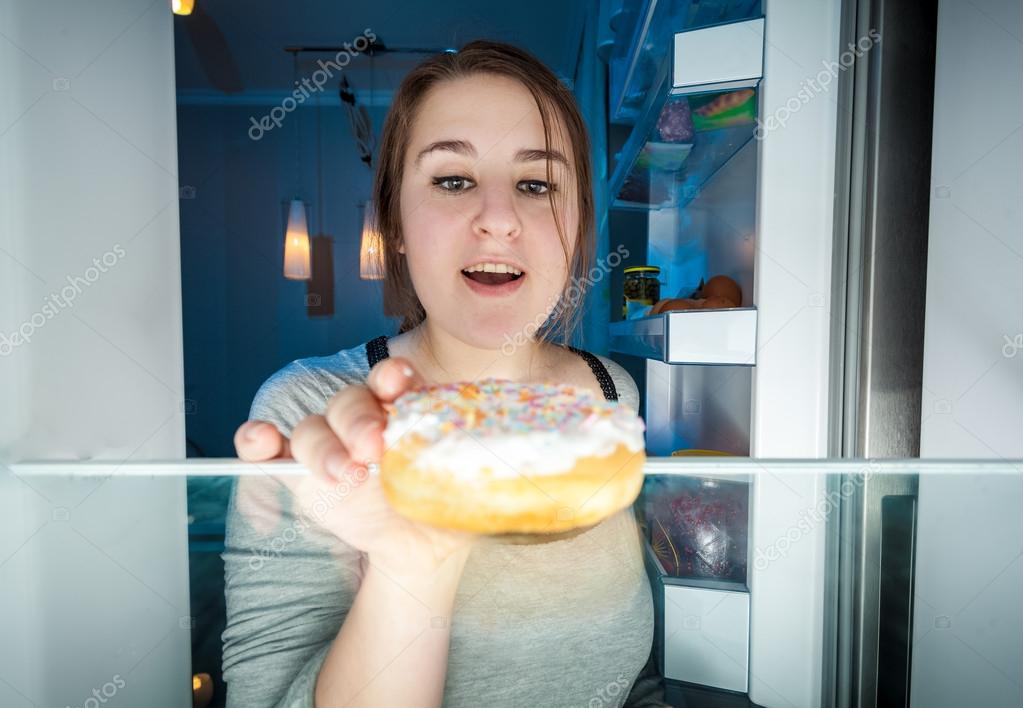 Young woman taking donut out of fridge at night — Stock Photo © Kryzhov ...