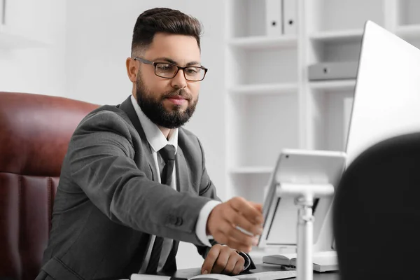 Handsome bank manager working with tablet computer at table in office ...