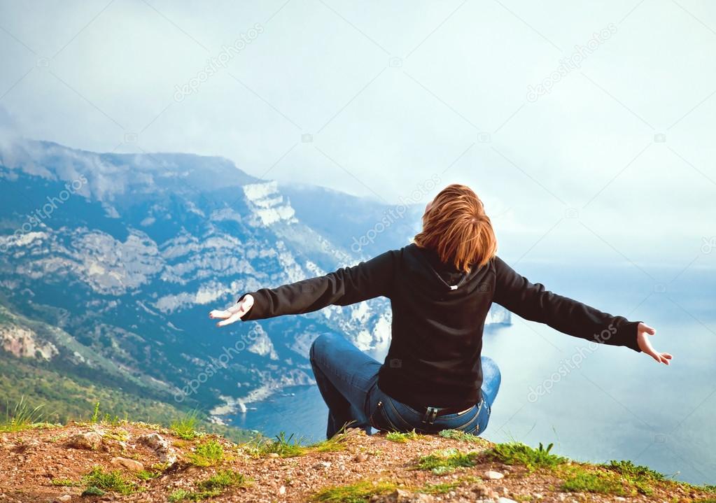 Young girl sitting on a hill overlooking the sea and mountains a ...