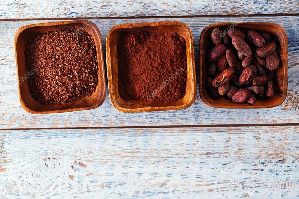 granos de cacao, polvo y chocolate rallado en tazones de madera, blanco 2024