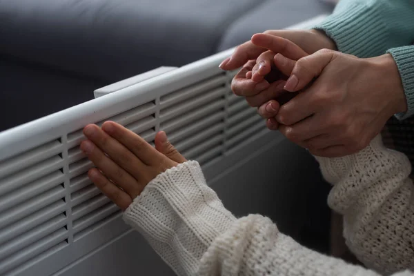 At the electric heater, people are warming themselves, covered with a ...