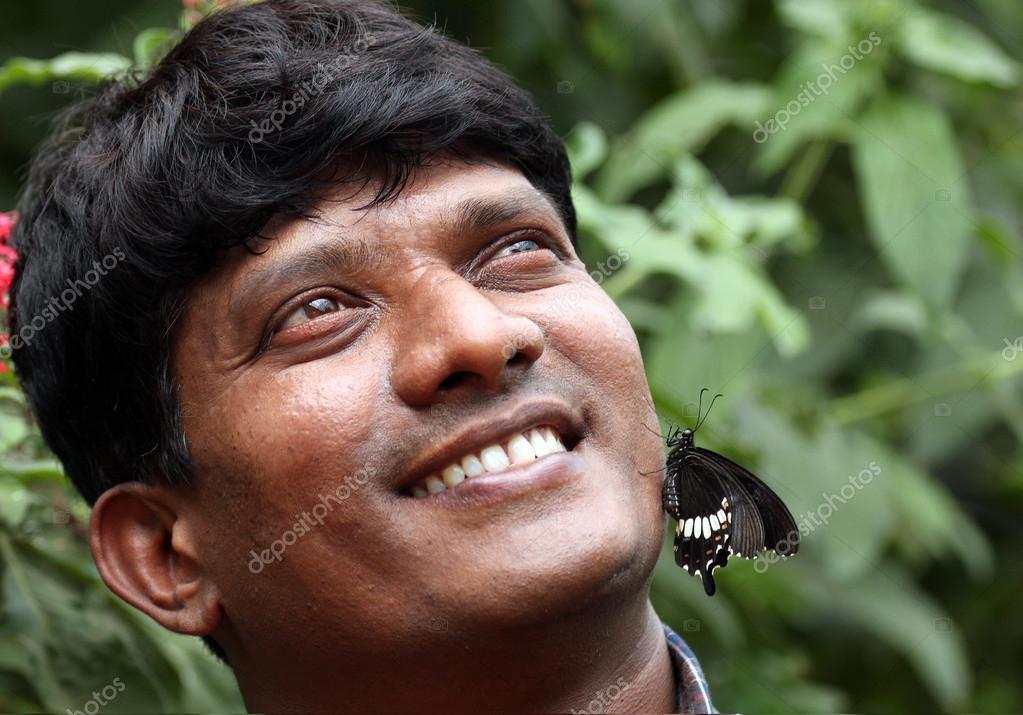 Guapo joven indio sonriendo con mariposa en la cara 2024