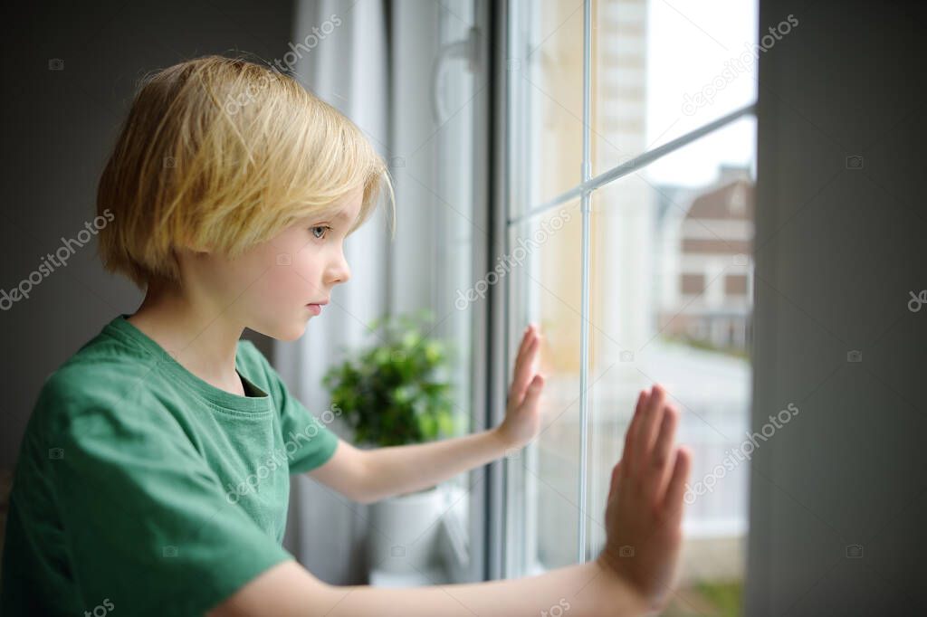 Sad little boy sitting near window and watching street. Post-traumatic ...