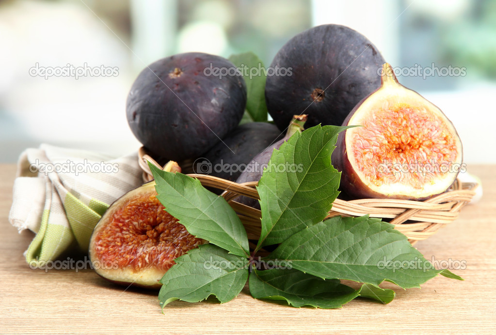 Ripe sweet figs with leaves in basket, on wooden table, on window ...