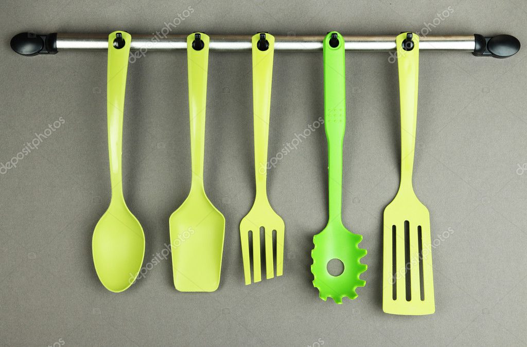 Plastic kitchen utensils on silver hooks on grey background — Stock ...