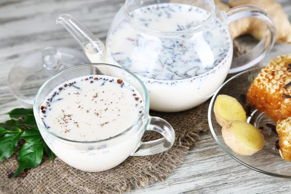 Teapot and cup of tea with milk and spices on sackcloth of wooden table ...