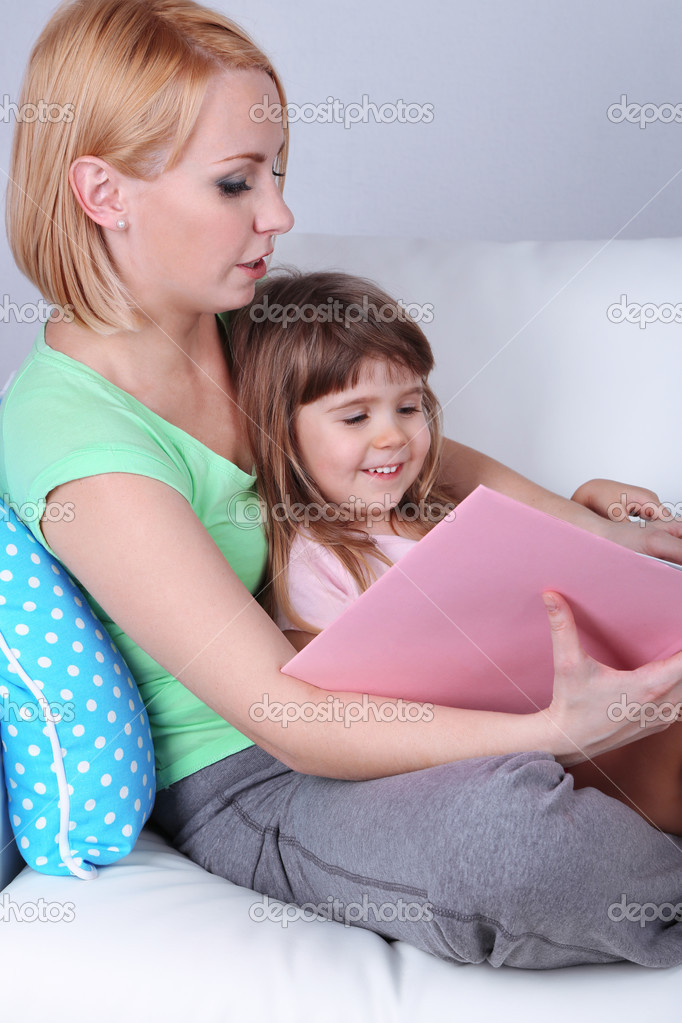 Pretty little girl reading book with mother on sofa on gray background ...