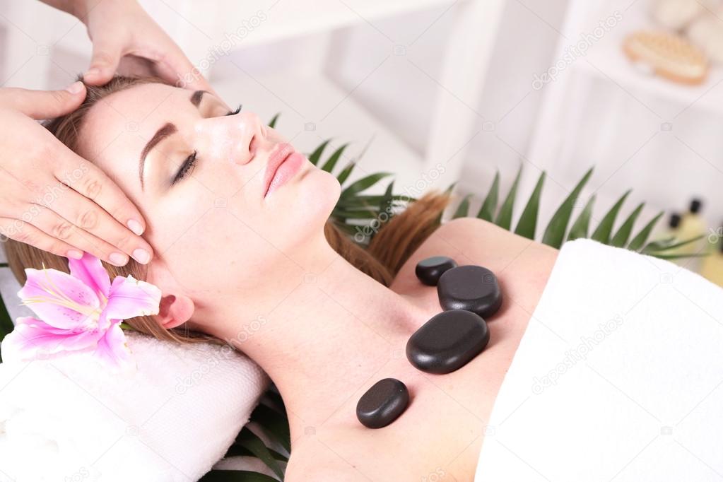 Hermosa mujer joven teniendo masaje de piedra en el salón de spa 2024