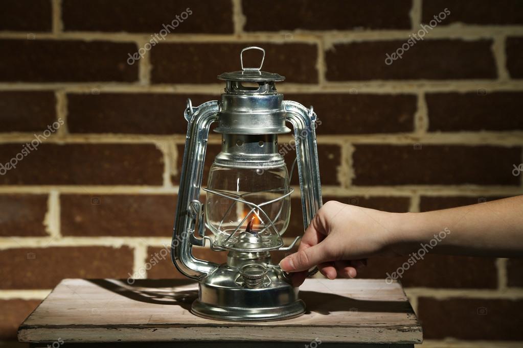 Hand lights a kerosene lamp on brick wall background — Stock Photo ...