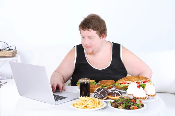 Fat man has a big lunch and playing games on laptop, on home interior ...