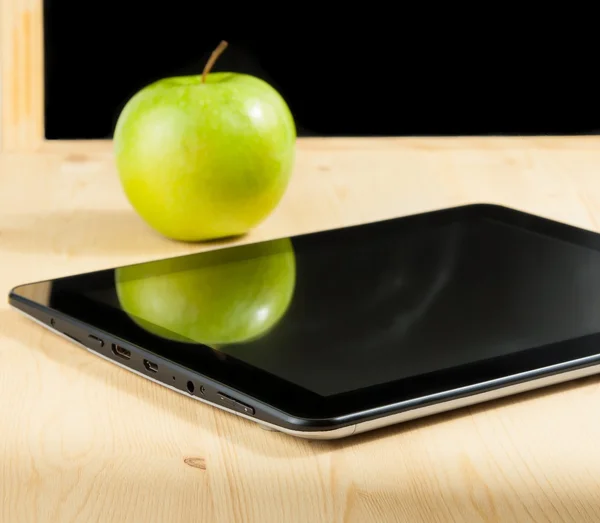 Digital tablet pc and green apple in front of blackboard on wood table ...